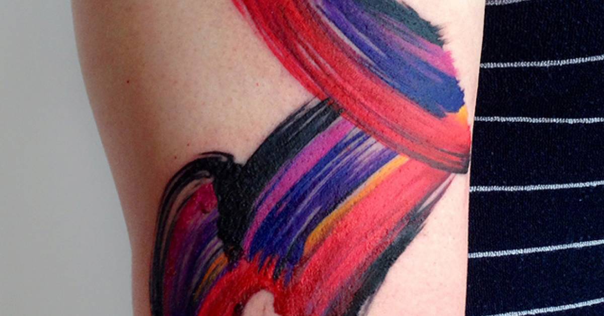 Abstract brushstroke tattoo on the right upper arm.