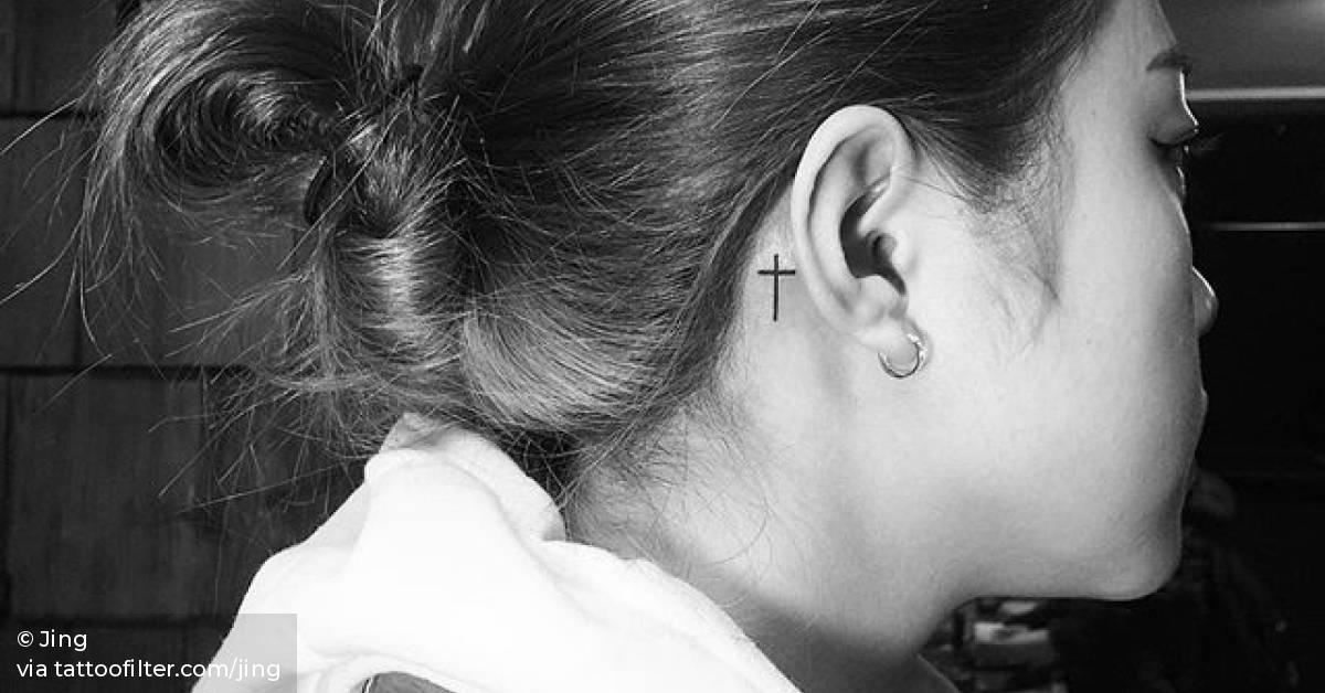 Minimalist cross tattoo behind the right ear.