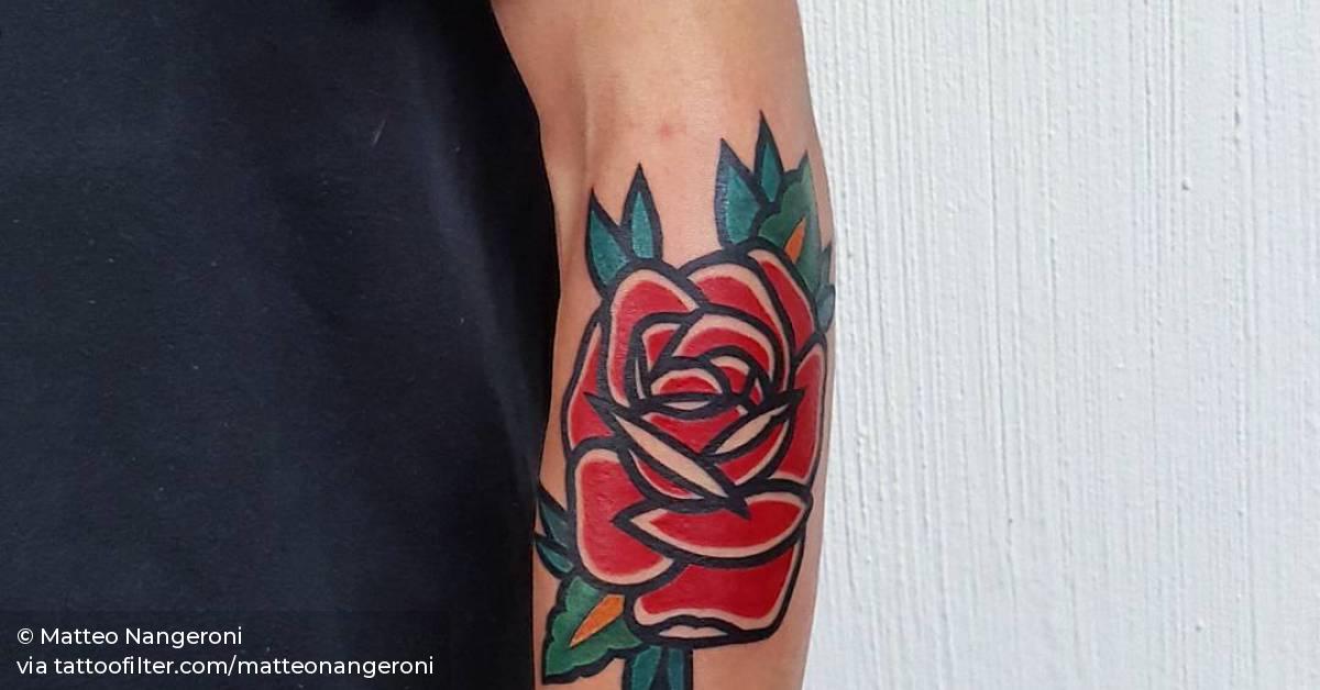 Bold traditional red rose tattoo on the left forearm.