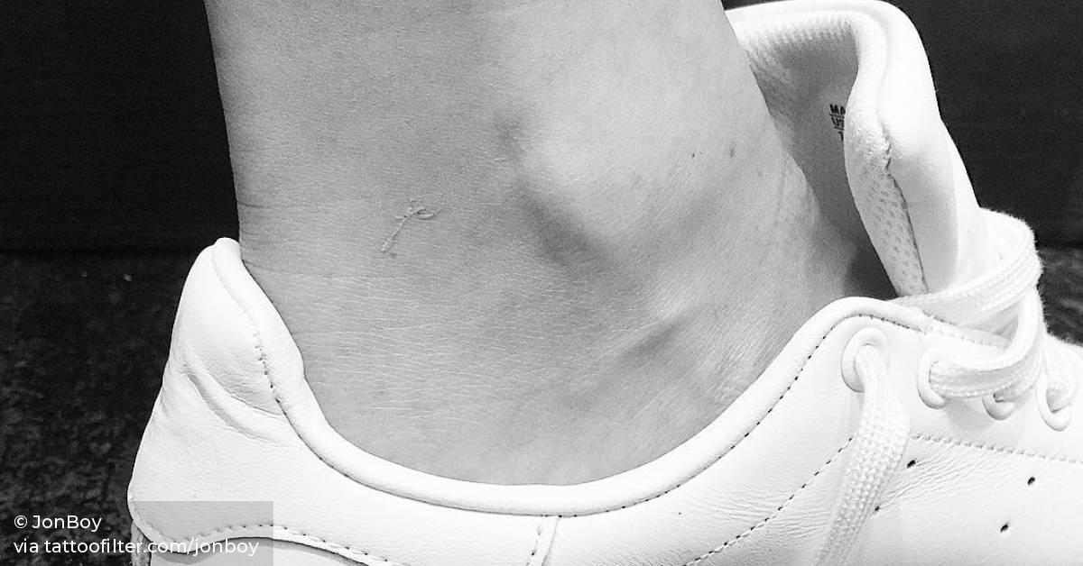 White ink "JC" tattoo on the ankle.