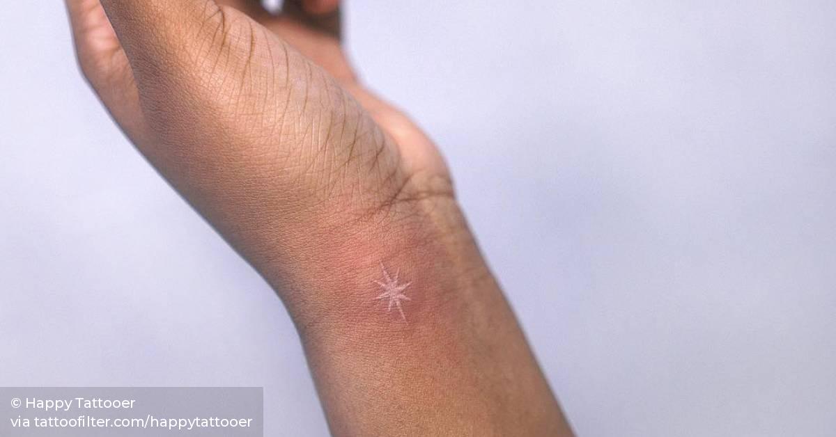 White ink star tattoo on dark skin.