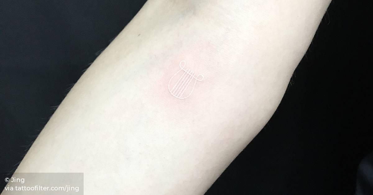 White ink lyre tattoo on the inner forearm.