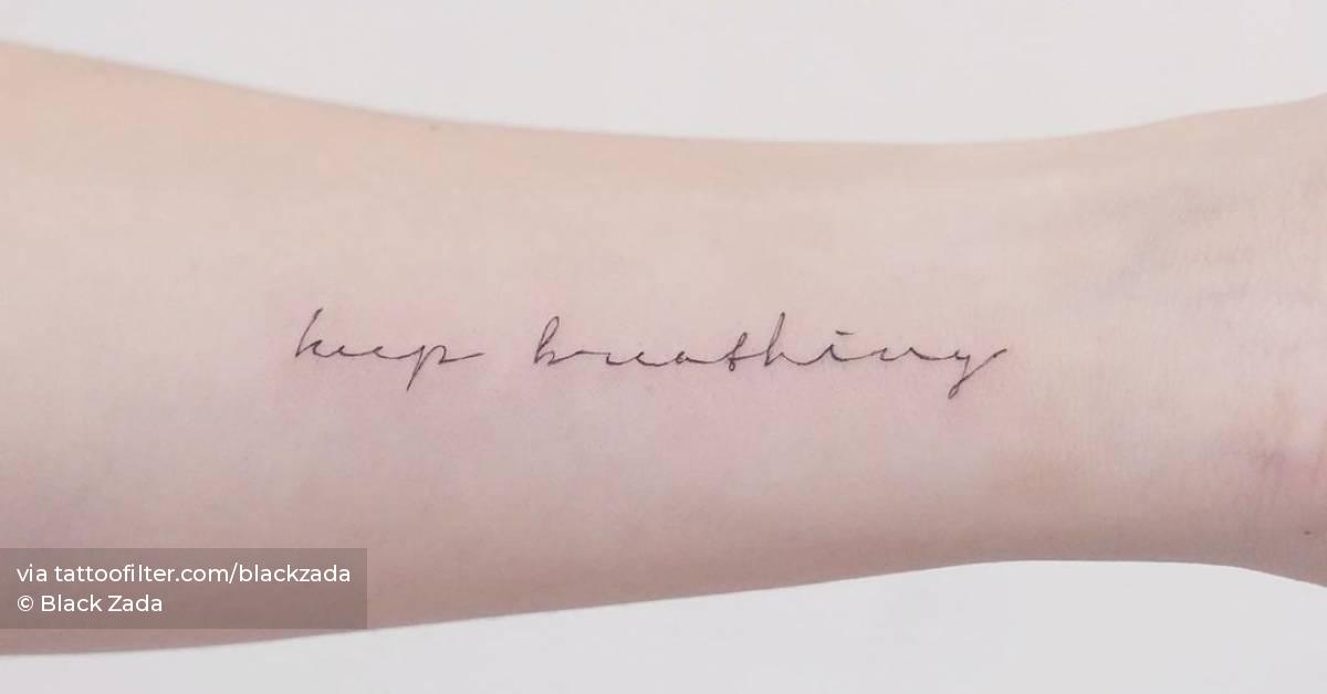 "Keep breathing" lettering tattoo on the inner forearm.