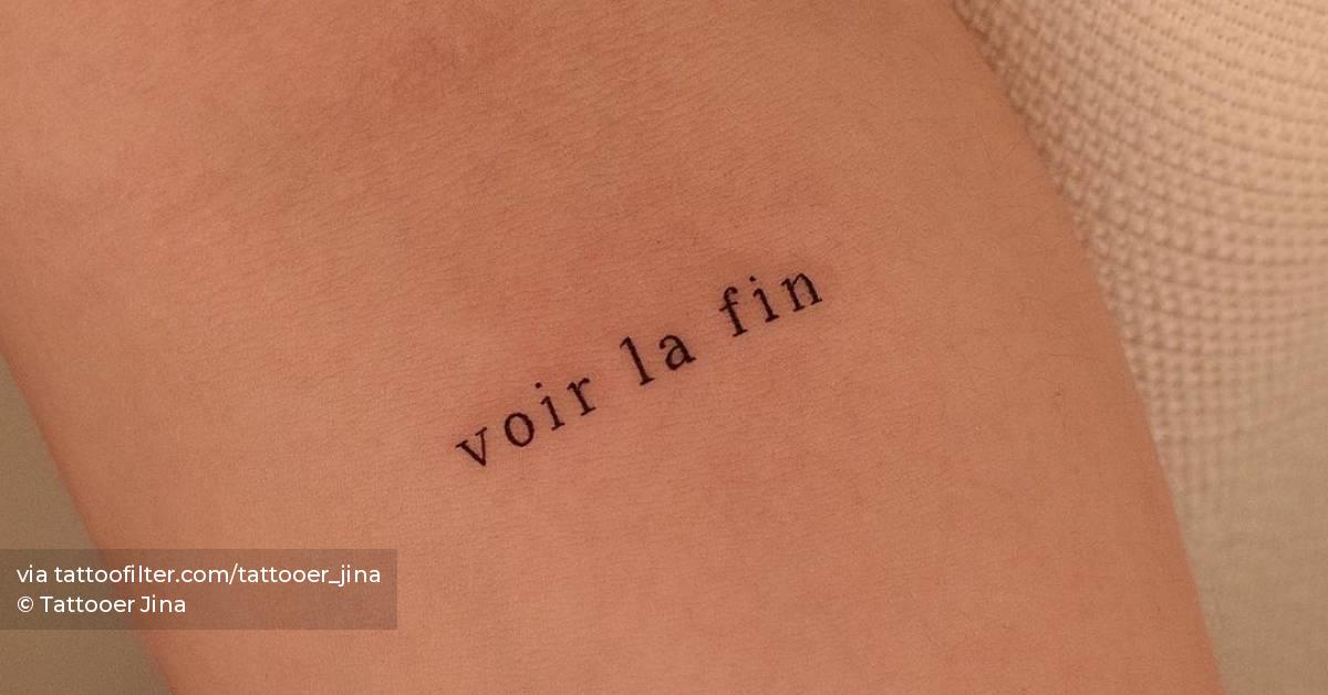 "Voir la fin" lettering tattoo on the inner forearm.