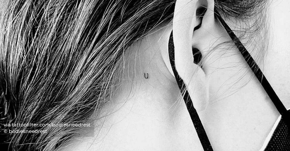 Minimalist letter "U" tattoo behind the ear.