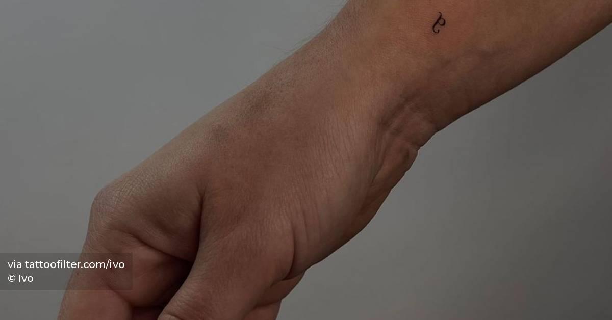 Minimalist letter "a" tattoo on the wrist.