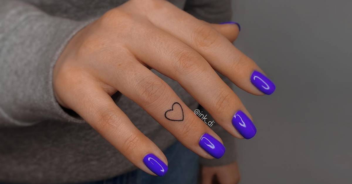 Tiny heart tattooed on the finger, minimalistic style.
