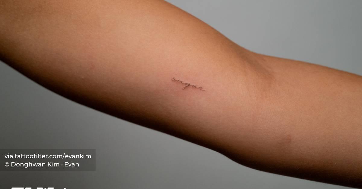 Tiny tattoo of the word "sugar" located onthe inner