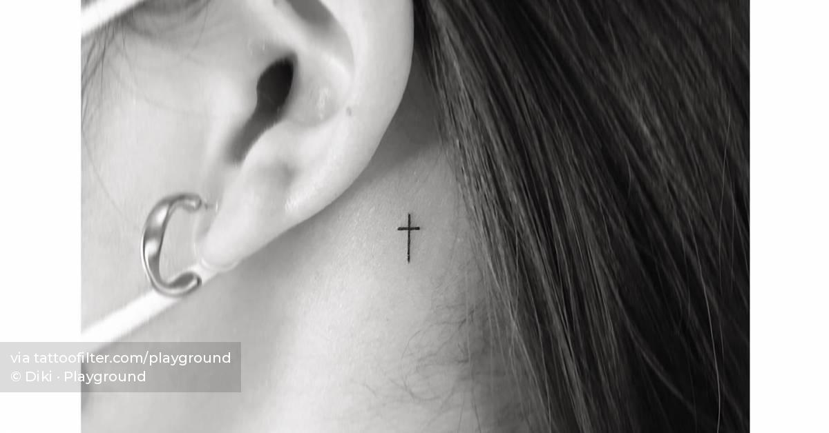 Minimalistic cross tattoo located behind the ear.