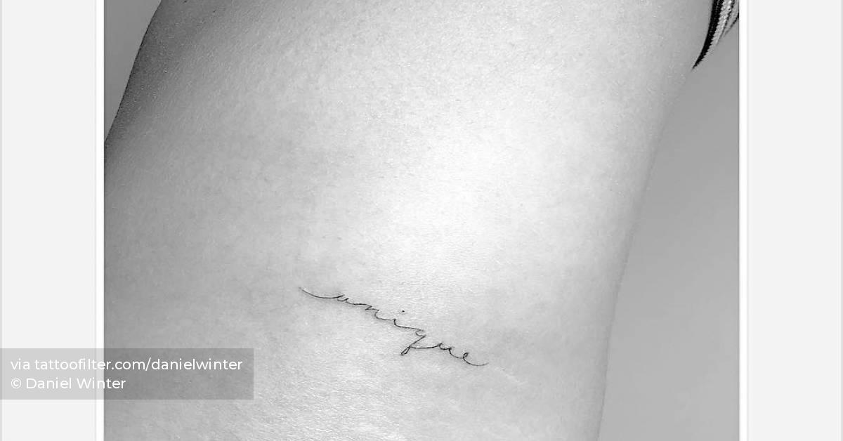 Tattoo of the word "unique" handwritten on the hip.