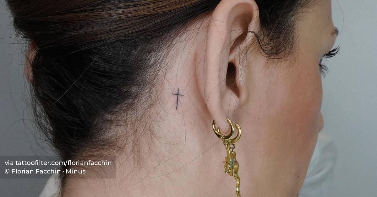 TIny cross tattoo located behind the ear.