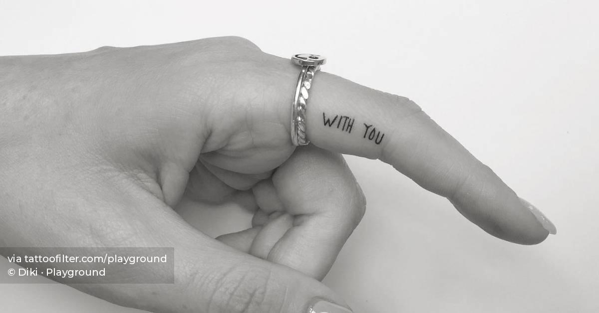 "With you" lettering tattoo on the finger.