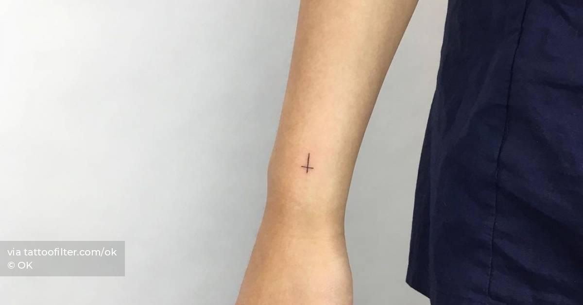 Minimalist cross tattoo on the wrist.