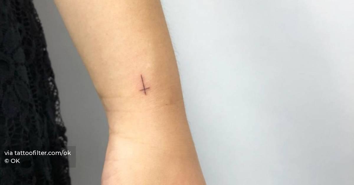 Minimalist cross tattoo on the wrist.