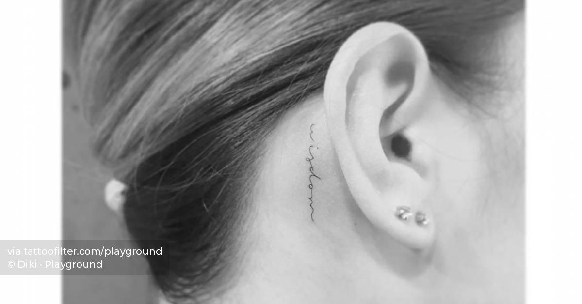 Tattoo of the word "wisdom" handwritten behind the ear.