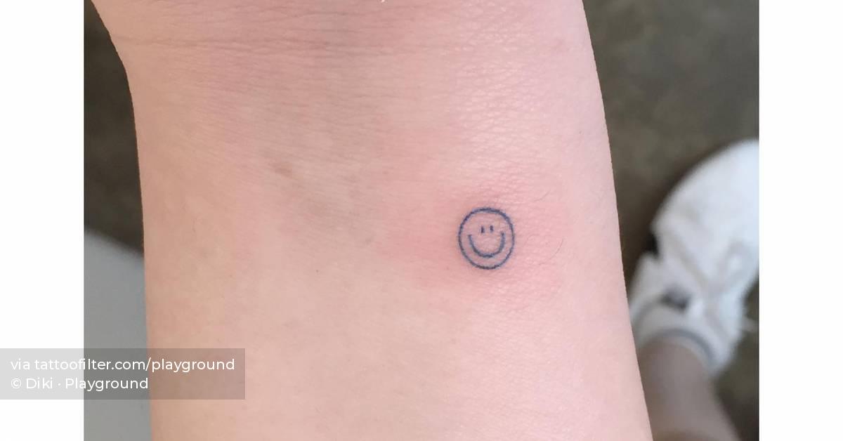 Minimalistic blue smiley face tattooed on the wrist.