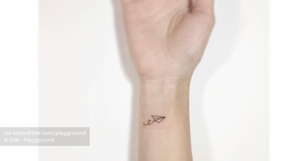 Fine line paper plane tattoo located on the wrist.