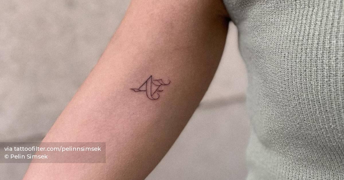 Fine line initials tattooed on the inner arm.