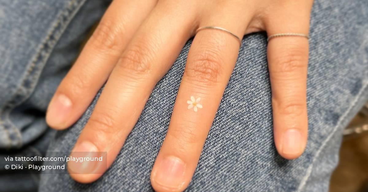 Micro daisy flower tattoo placed on the finger.