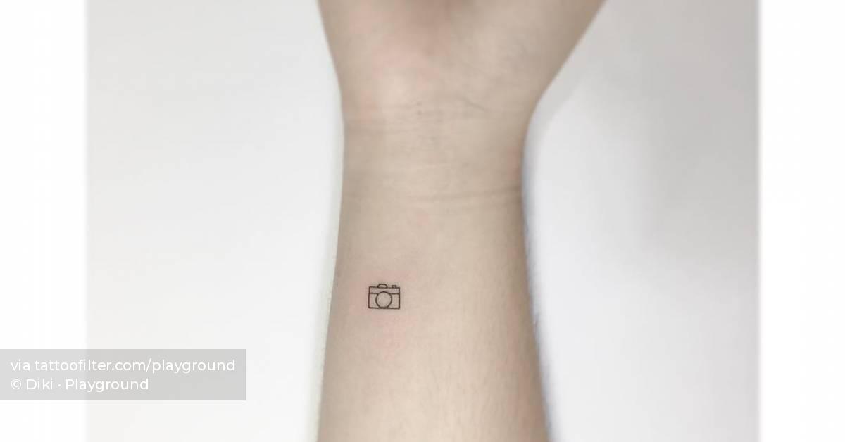 Tiny fine line reflex camera tattooed on the wrist.