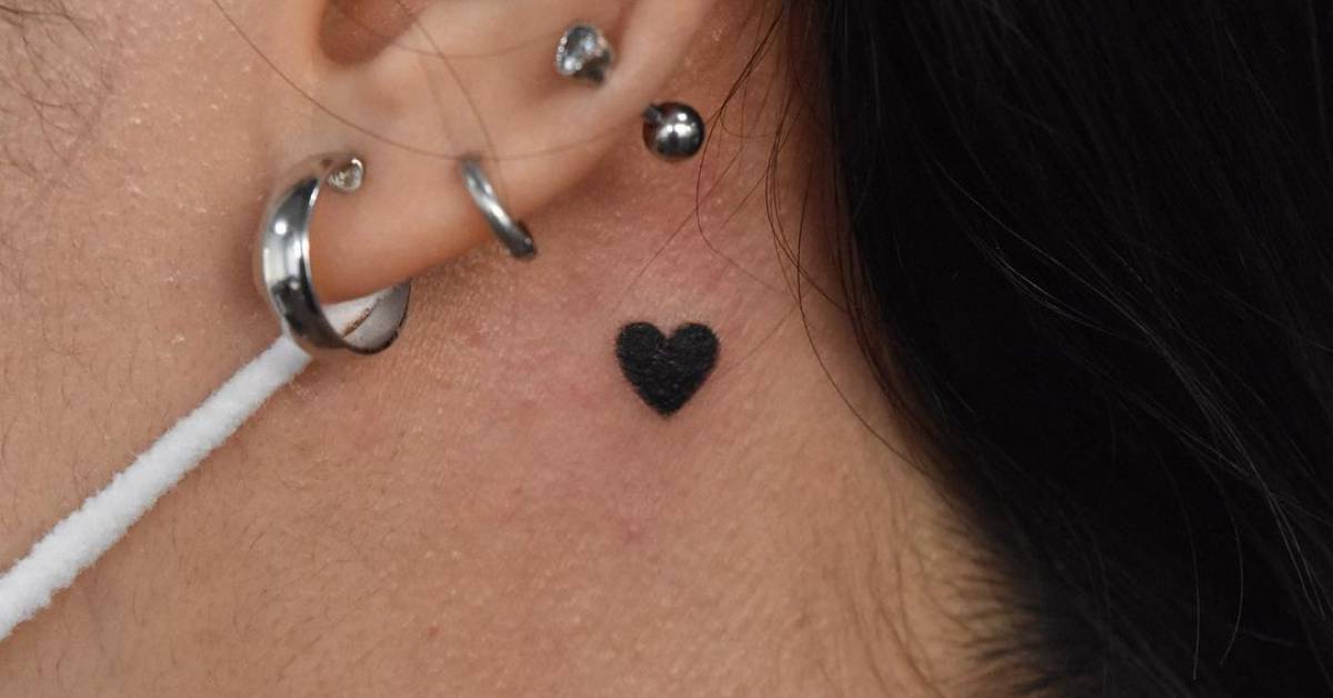 Minimalistic style heart tattoo located behind the ear.