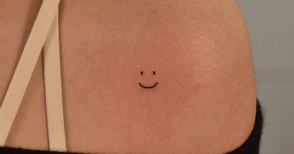 Mini smiley face tattoo located on the shoulder blade.