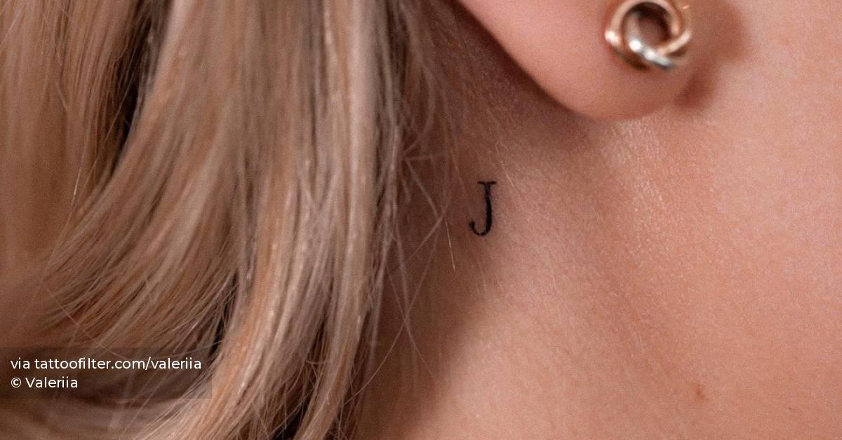 Mini letter "J" tattoo located behind the ear.