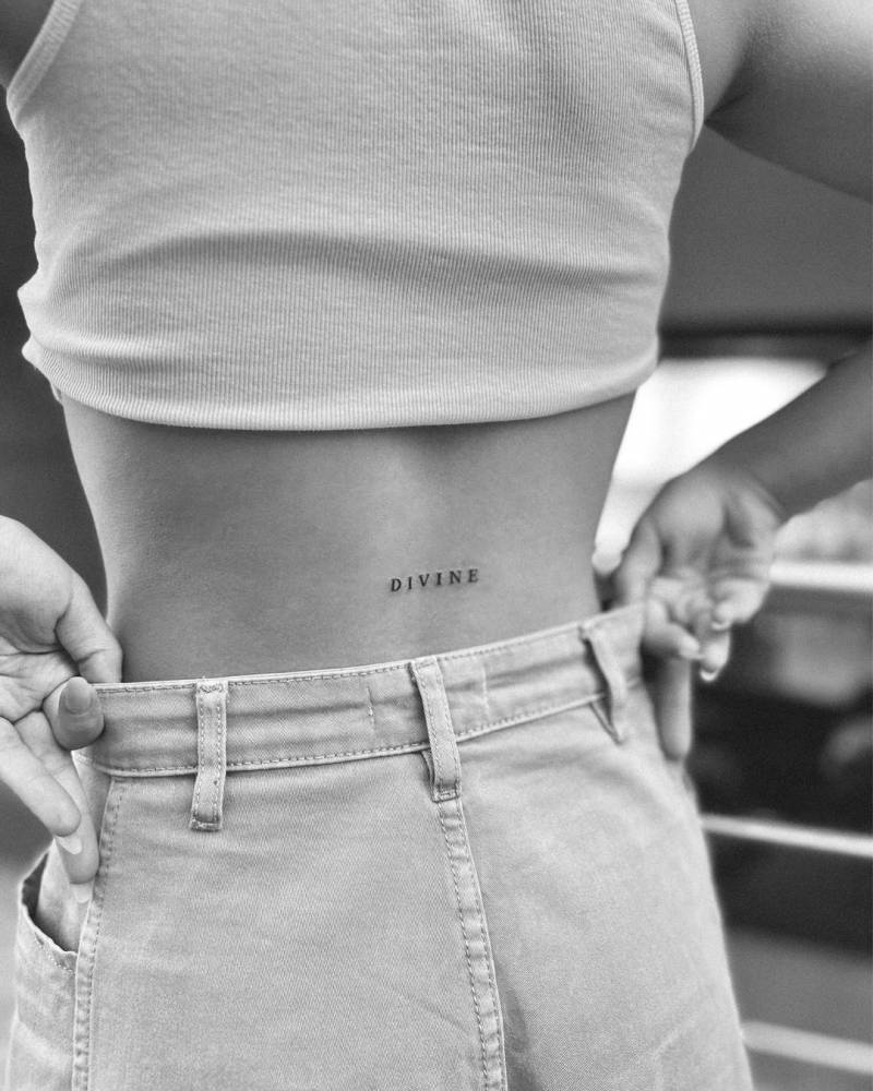 Tattoo Of The Word divine Located On The Lower Back 