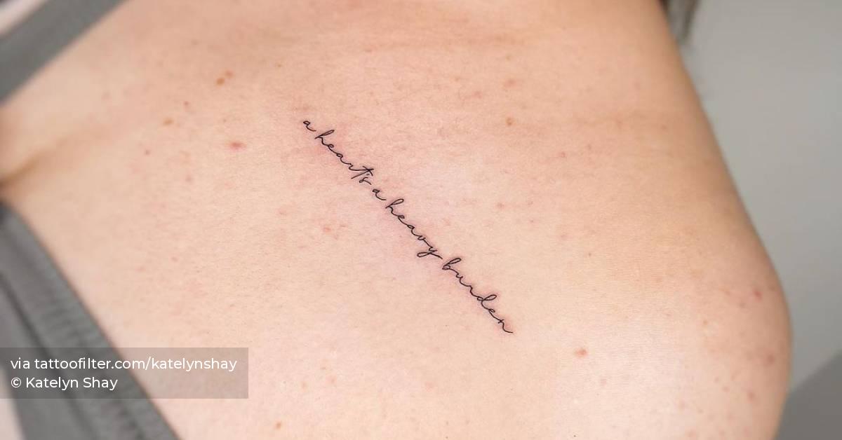 "A heart is a heavy burden" lettering tattoo located on