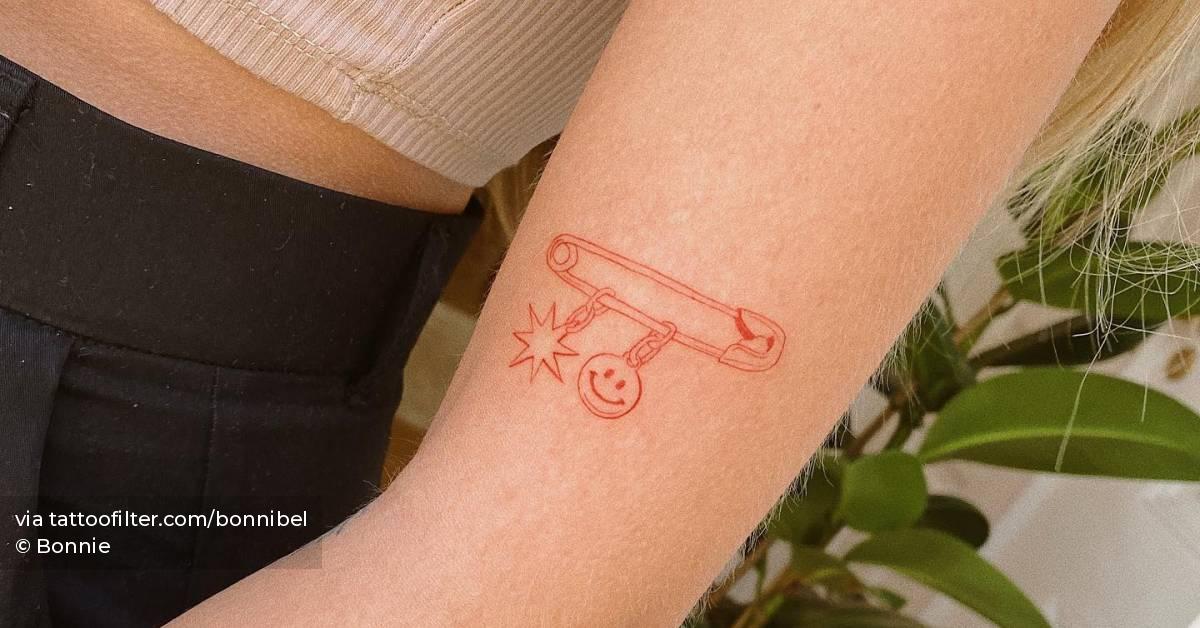 Safety pin tattoo located on the upper arm, done in red