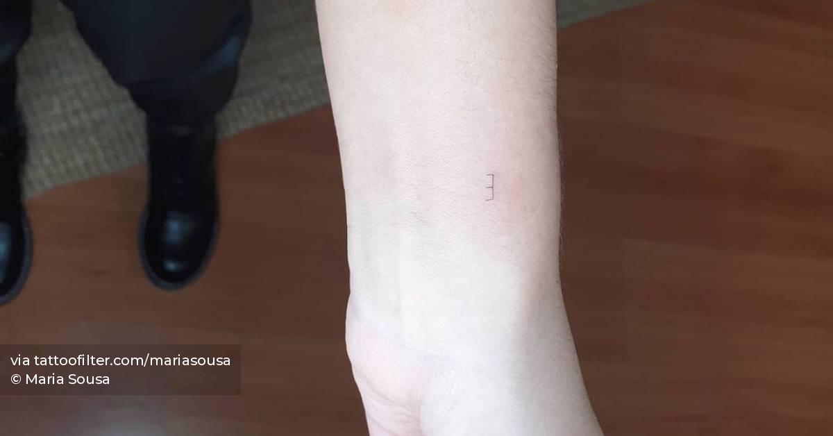 Minimalist letter "E" tattoo on the wrist.