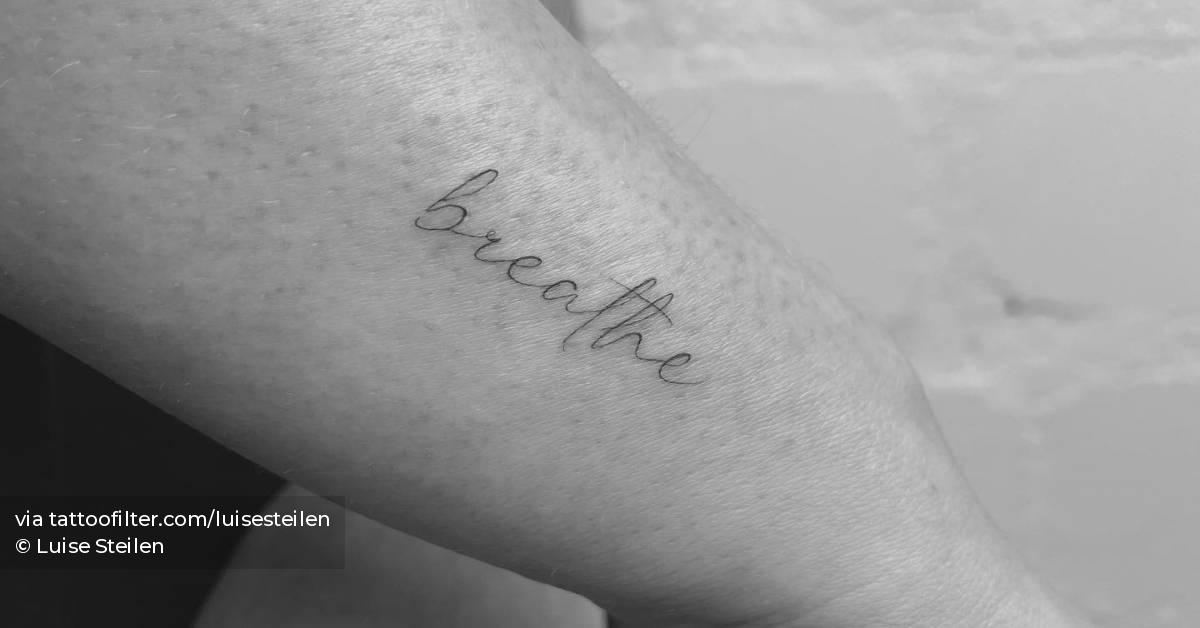 Word "breathe" tattoo handwritten on the wrist.