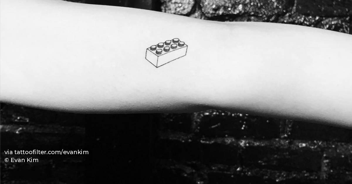 Lego piece tattooed on the inner arm, fine line style.