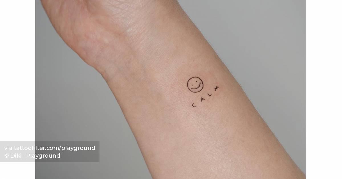 Smiley face and the word "calm" tattoed on the wrist.