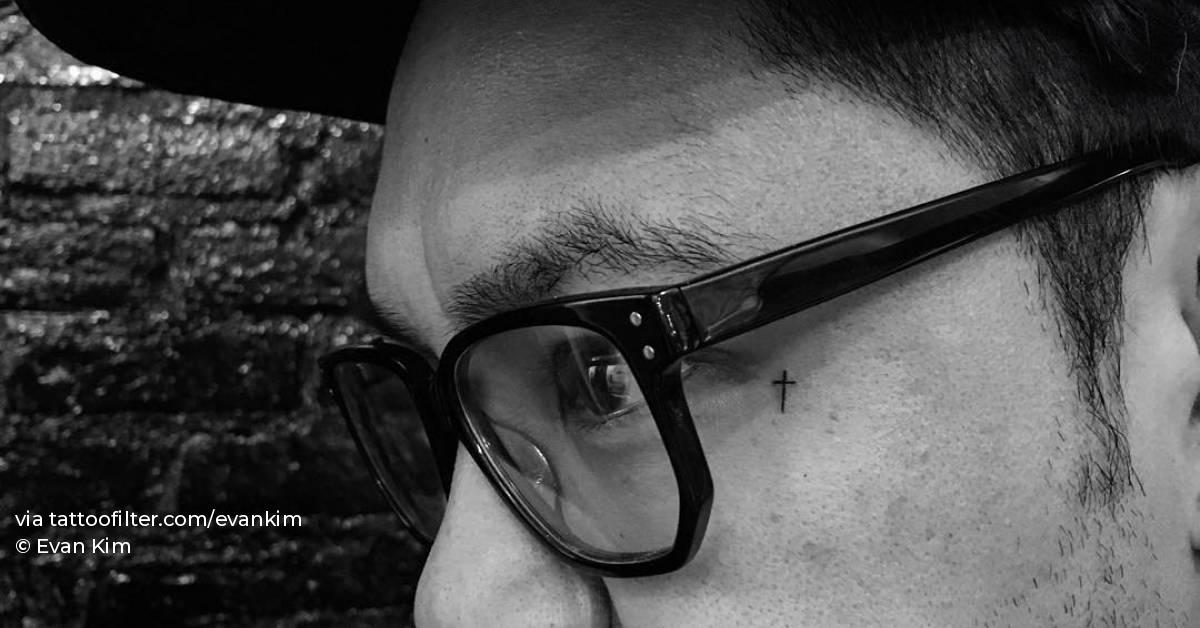 Minimalistic cross tattoo done on JonBoy's face.