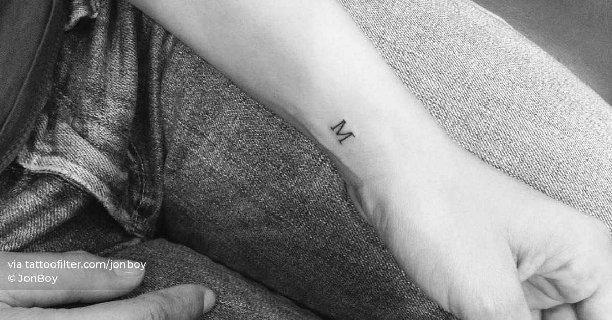 Minimalistic style letter "M" tattoo located on the