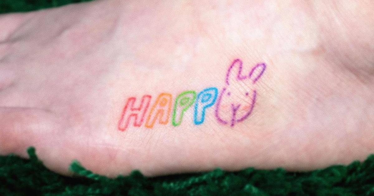 Tattoo of the word "happy" with a bunny face located on