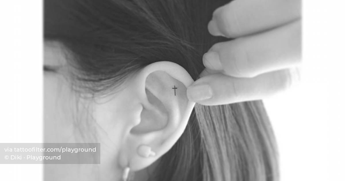 Tiny minimalistic cross tattoo located on the ear.