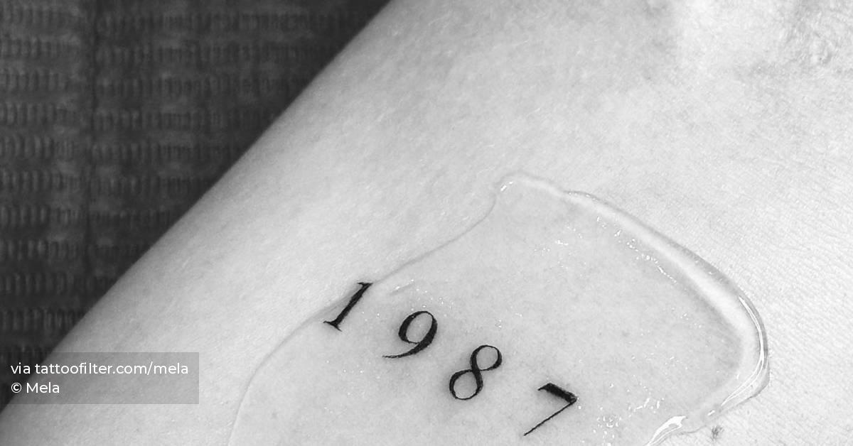 "1987" lettering tattoo located on the inner forearm.