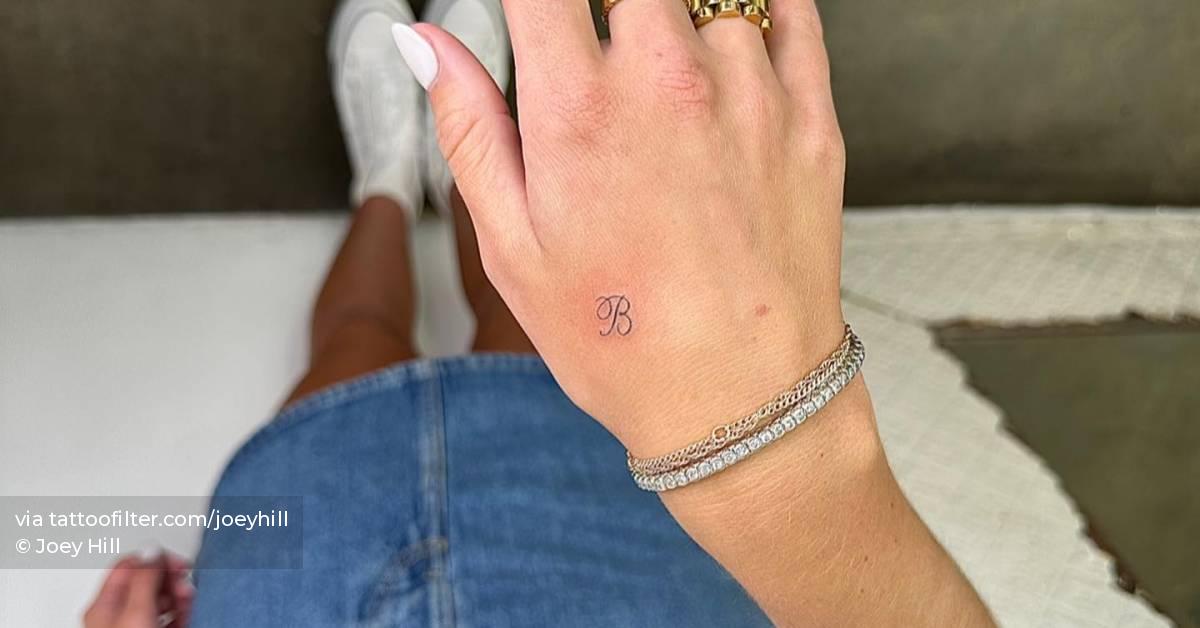 Tiny letter "B" tattoo done on the hand.