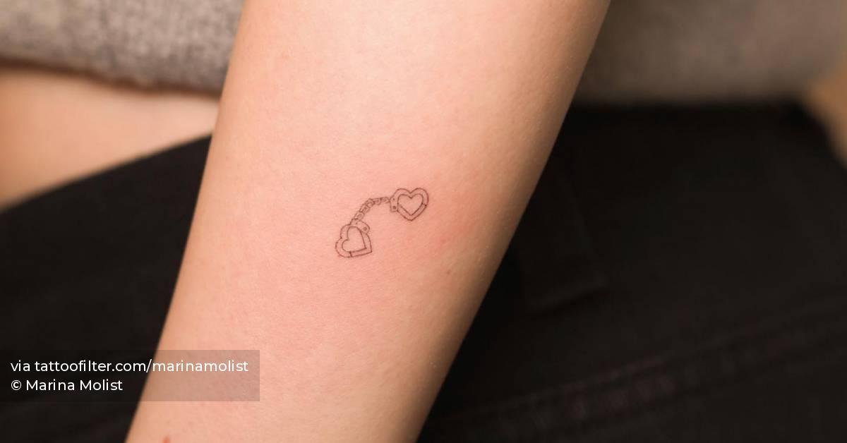 Heart shapped handcuffs tattooed on the forearm, fine