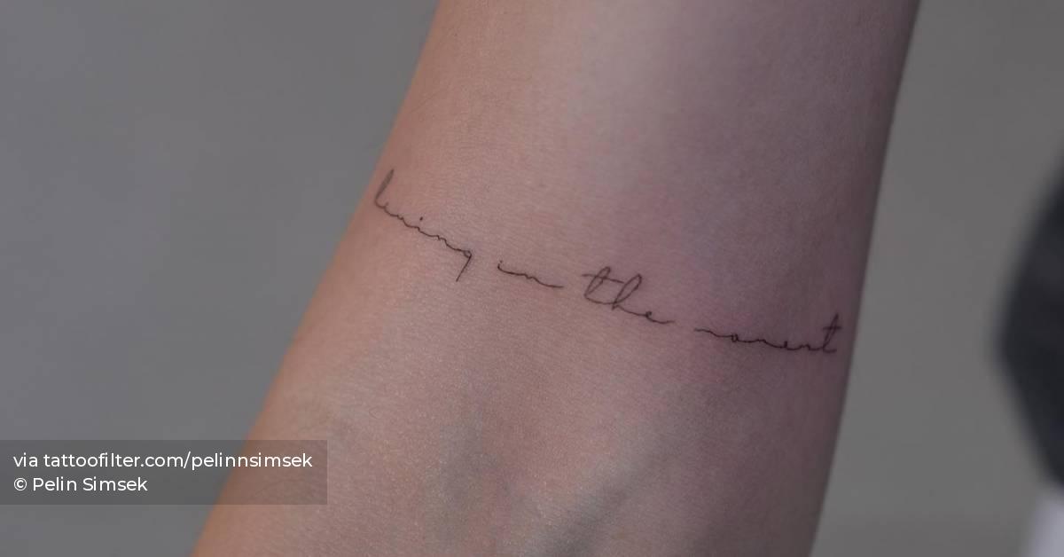 Tattoo that says "living in the moment" handwritten on