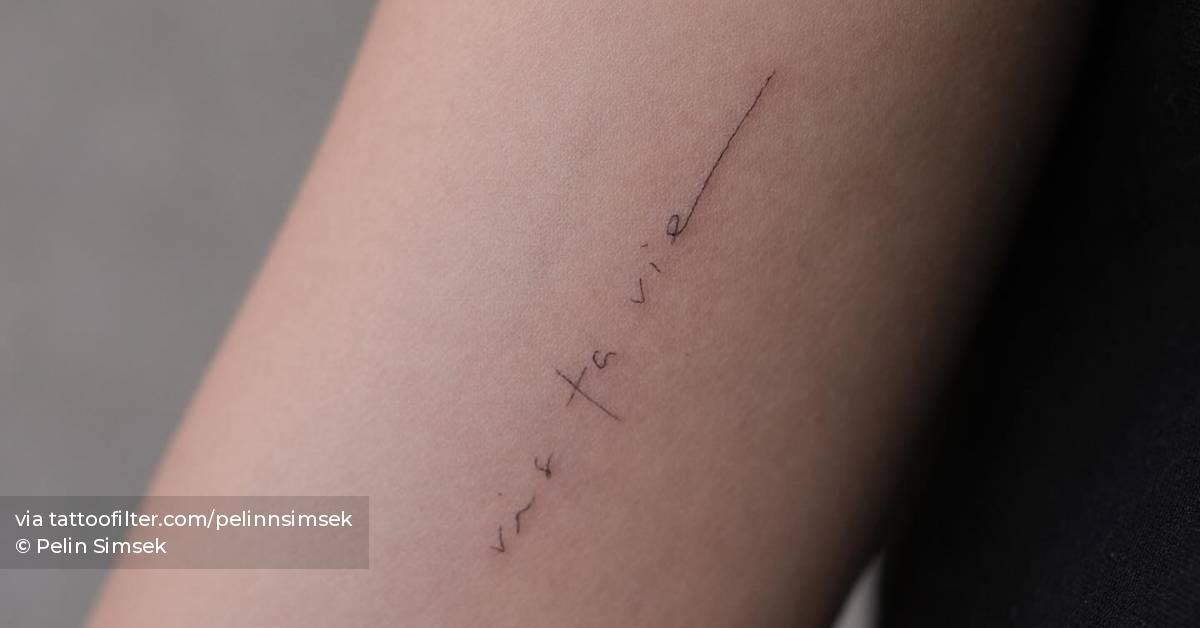 "Vis ta vie" lettering tattoo located on the inner arm.