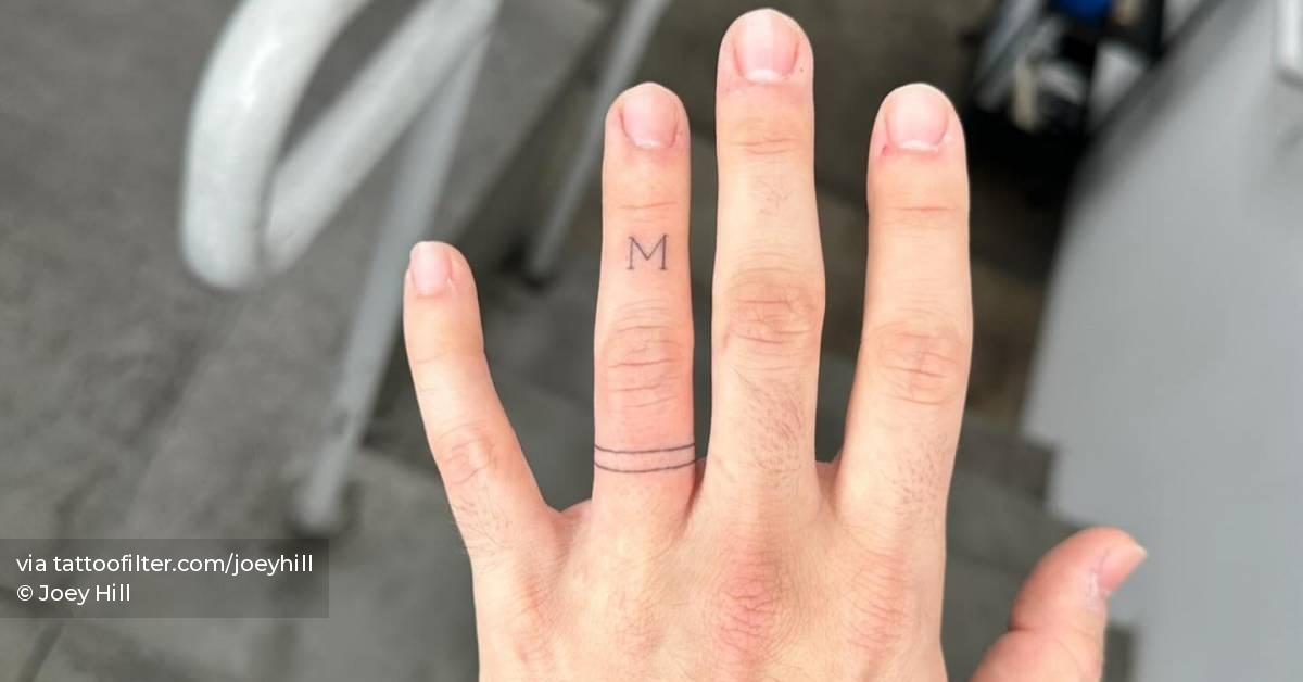 Tiny letter "M" and ring tattooed on the finger.