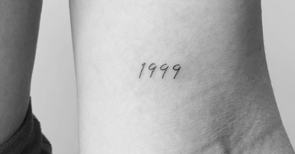 Tiny "1999" lettering tattoo located on the inner arm.