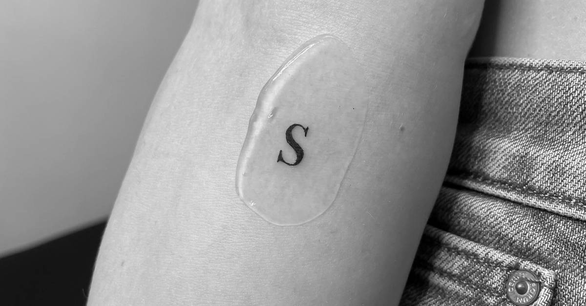 Tiny minimalistic tattoo of the letter "S" located on