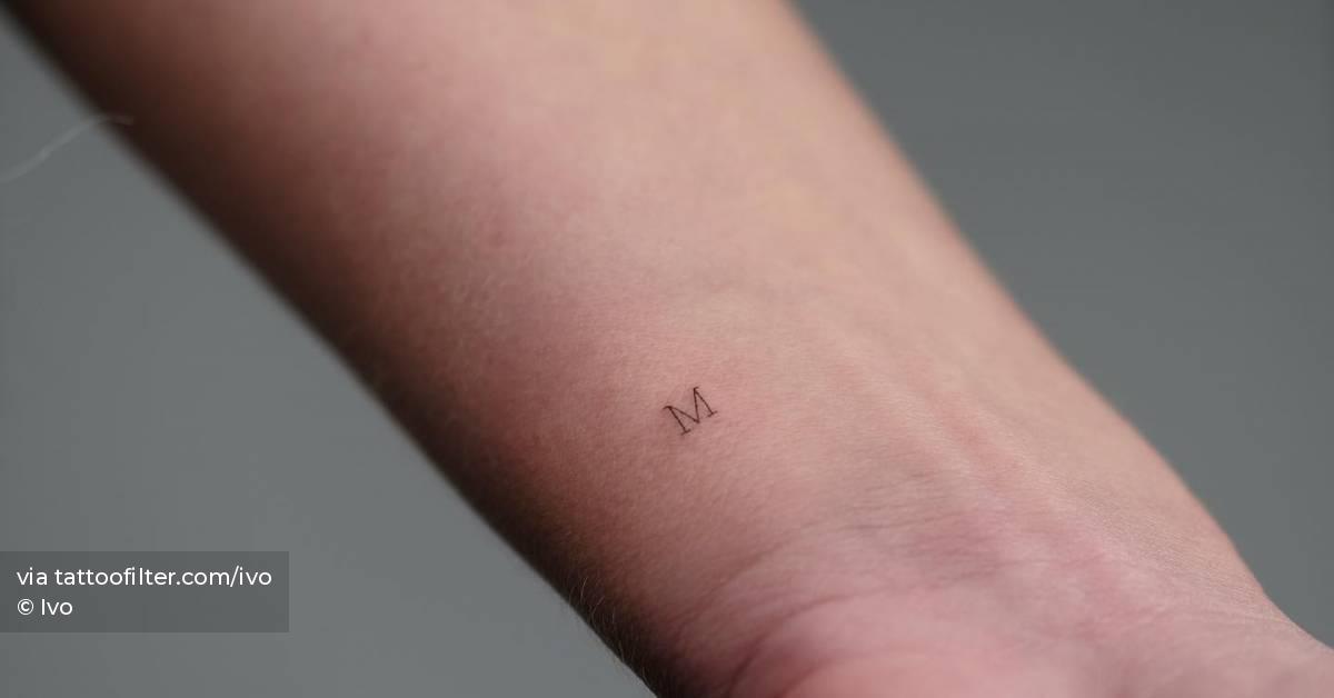 Tiny minimalistic letter "M" tattoo located on the