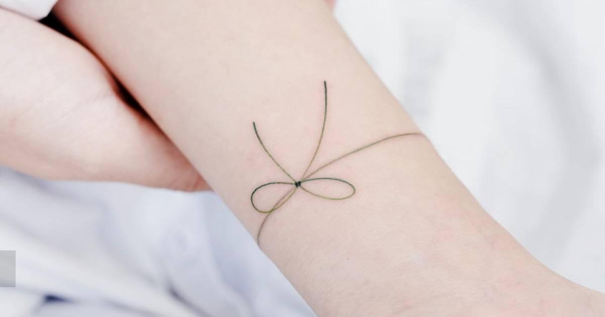 Ribbon wristband tattoo done in fine line style.