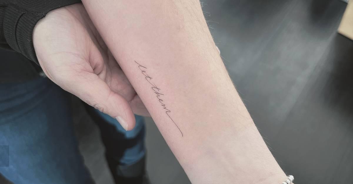 "Let them" lettering tattoo handwritten on the wrist.