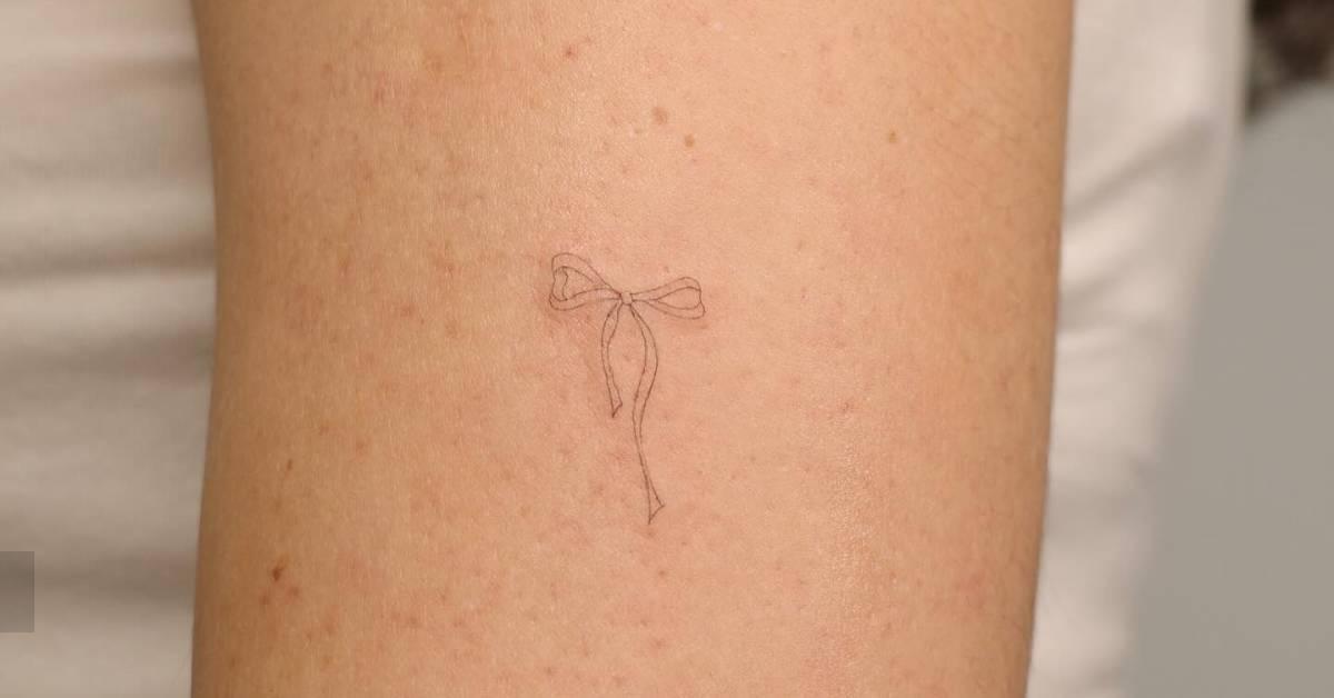 Ribbon tattoo placed on the upper arm, fine line style.